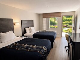 Quarto de hotel com duas camas, uma mesa de trabalho e vista para um jardim.