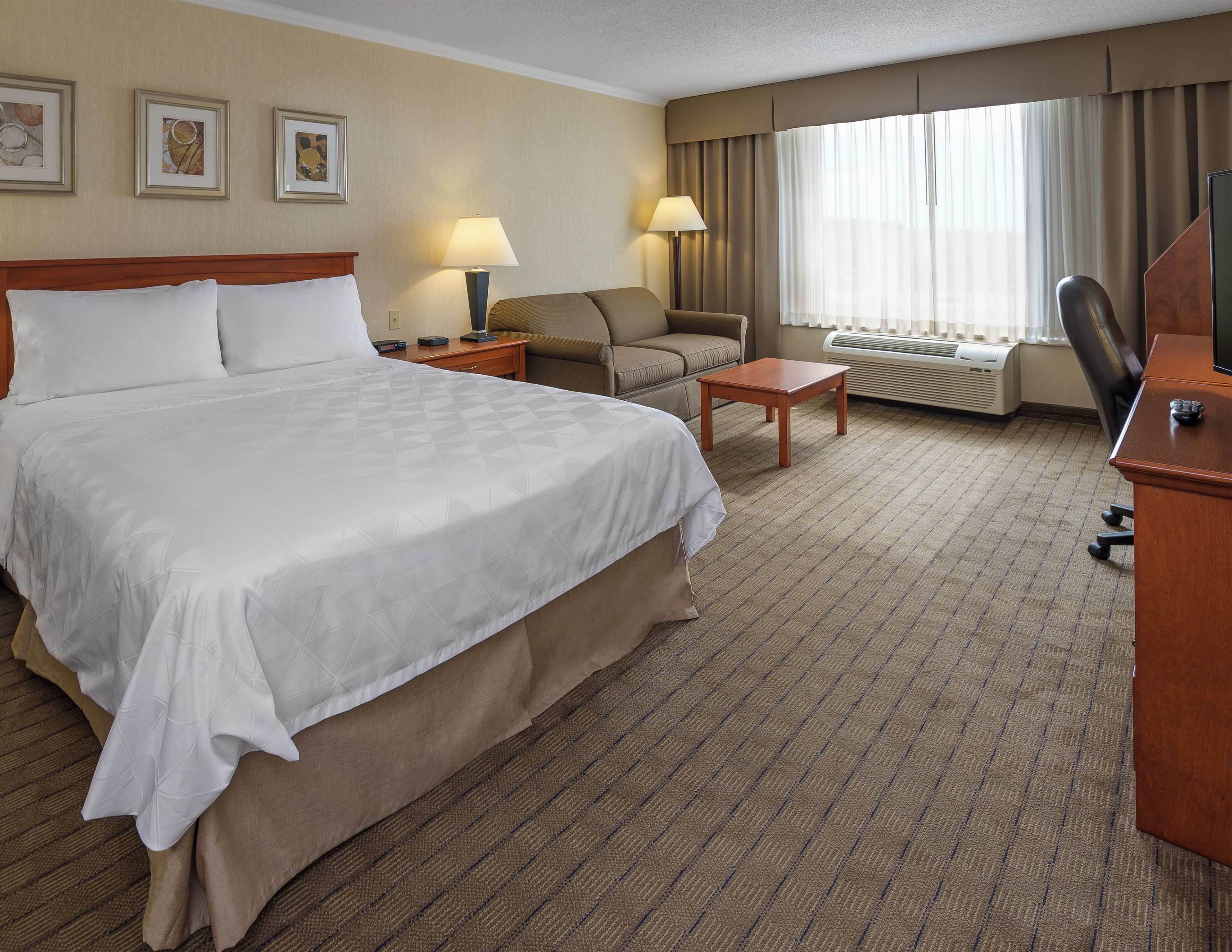 Quarto de hotel com uma cama grande, uma escrivaninha, uma cadeira, um sofá e uma janela com cortinas.
