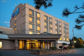 Hotel com fachada moderna, entrada desobstruída e placa indicando altura livre de 2,7 metros.