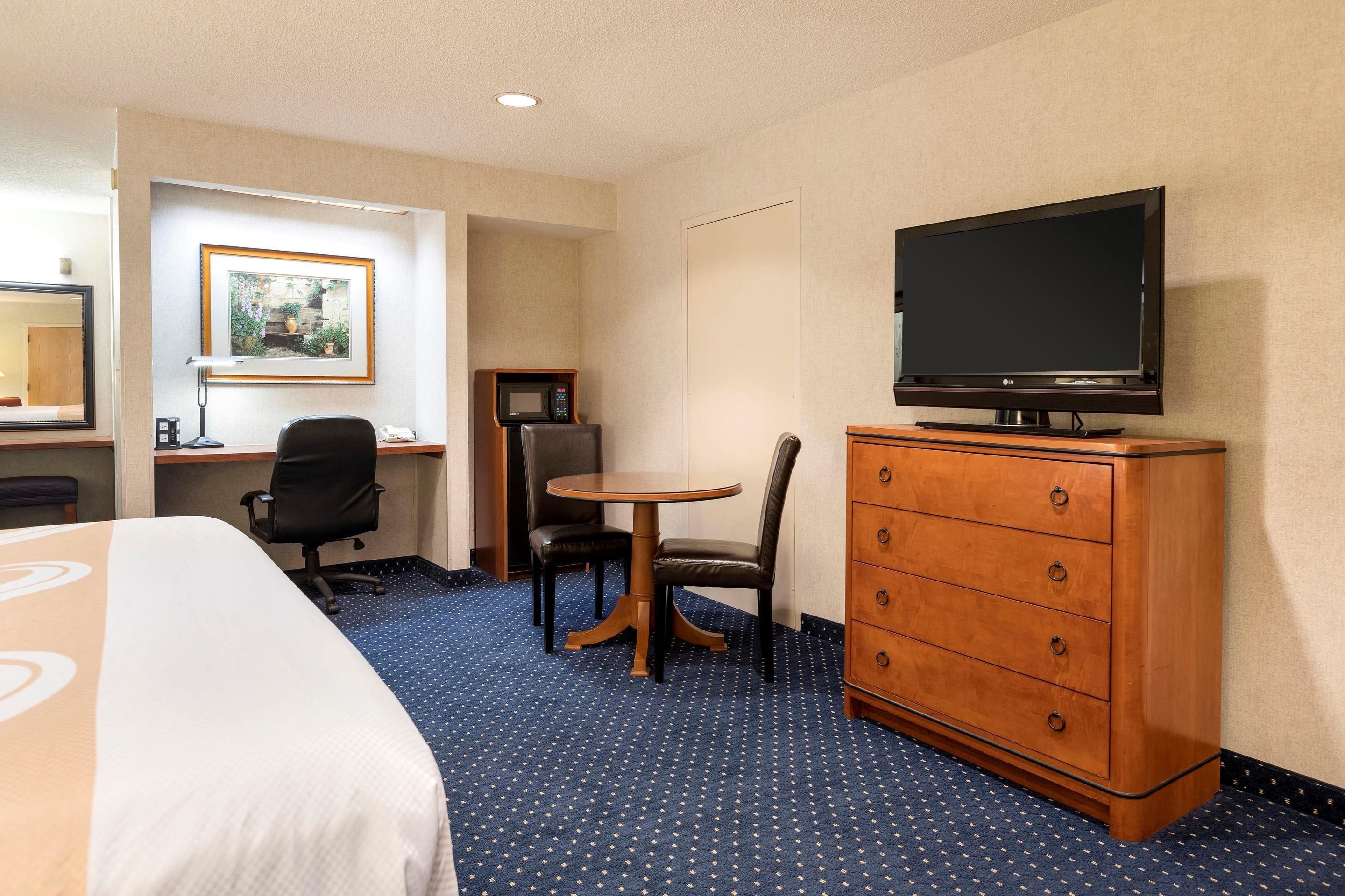 Quarto de hotel com cama, escrivaninha, cadeira, televisão e cómoda.