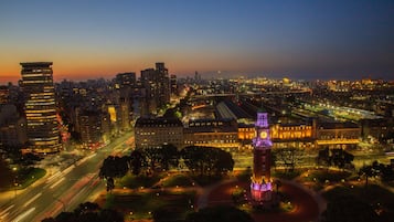 Paisagem urbana ao anoitecer, com prédios iluminados e uma torre do relógio imponente.