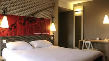 Quarto de hotel com cama, mesa de cabeceira, escrivaninha e espelho.