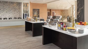 Espaço de café da manhã moderno com balcões de buffet, diversas opções de alimentos e um painel decorativo.