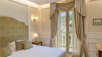 Quarto de hotel com uma cama grande, uma mesa de cabeceira com abajur e vista para uma varanda com cortinas.