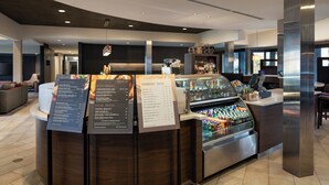 Um lobby moderno de hotel com um bar de café, área de estar e balcão de recepção.