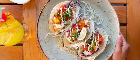 Um prato com três tacos sobre uma mesa de madeira.
