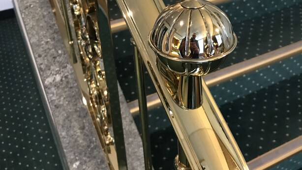 Uma escadaria com corrimão dourado e guarda-corpo de vidro.