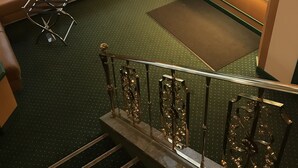 Um hall de hotel com balcão de recepção, um sofá, uma poltrona e uma escada.
