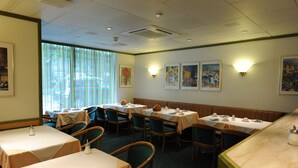 Restaurante com várias mesas e cabines, cada uma com toalhas de mesa brancas e cadeiras verdes.