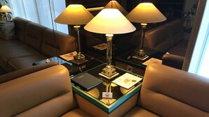 Uma área de estar no canto com dois poltronas de couro, uma mesa de vidro com um livro e um certificado, e três luminárias de mesa.