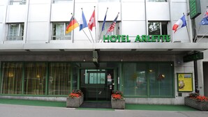 Entrada de hotel com várias bandeiras, toldo verde e placa com a inscrição "HOTEL ARLETTE".