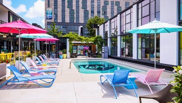 Uma área de piscina ao ar livre com espreguiçadeiras e guarda-sóis, cercada por edifícios.