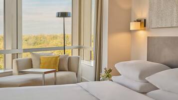 Quarto de hotel com cama, sofá, mesa pequena, abajur e vista para o exterior.