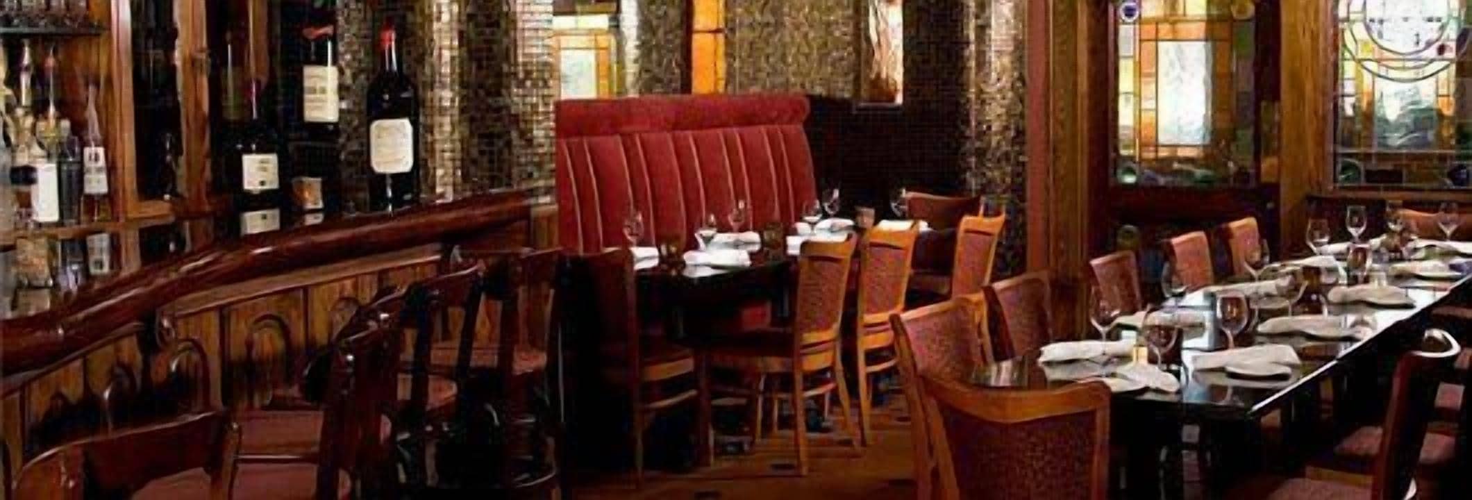 Um restaurante com uma mesa de jantar comprida, cabines estofadas em vermelho e um bar com garrafas.