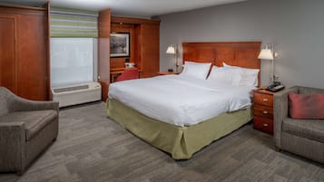 Quarto de hotel com uma cama grande, duas mesinhas de cabeceira, uma escrivaninha com cadeira e uma janela com persianas.