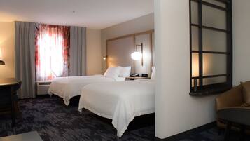 Quarto de hotel com duas camas, uma escrivaninha, uma cadeira e uma janela grande com cortinas.