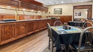 Espaço de refeições de hotel com painéis de madeira, sistema de buffet e uma mesa posta para quatro pessoas, com cadeiras.