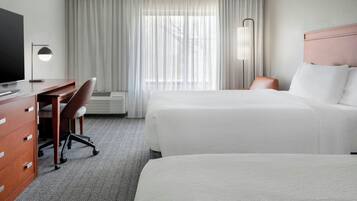 Quarto de hotel com cama, escrivaninha, cadeira, televisão e luminária.