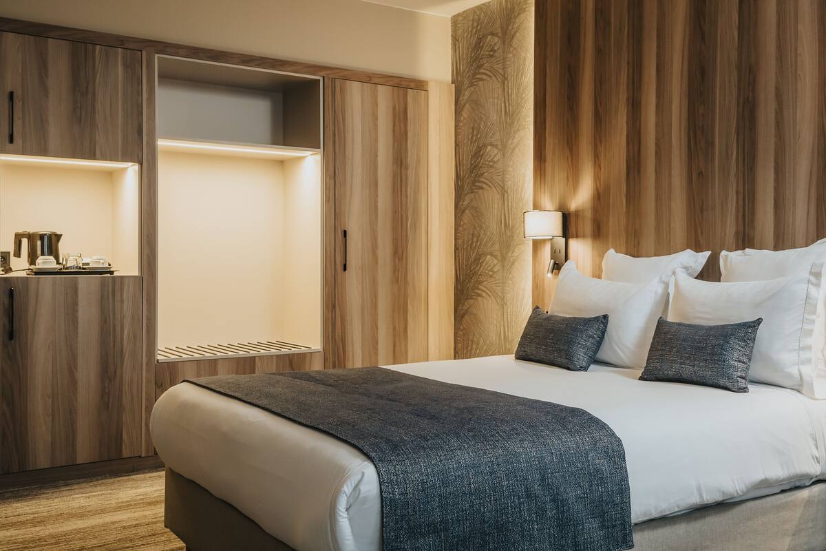 Quarto de hotel com uma cama grande, um guarda-roupa com espelho e uma mesa de cabeceira com abajur.