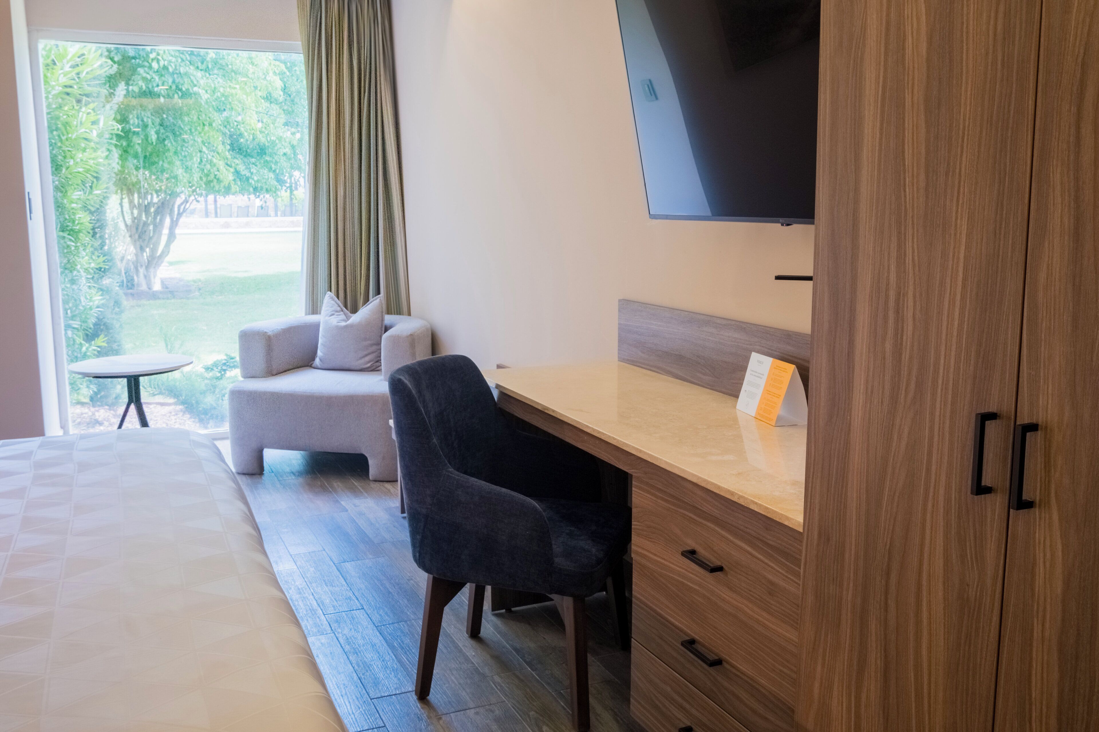 Quarto de hotel com cama, escrivaninha, poltrona, televisão e vista para o exterior.