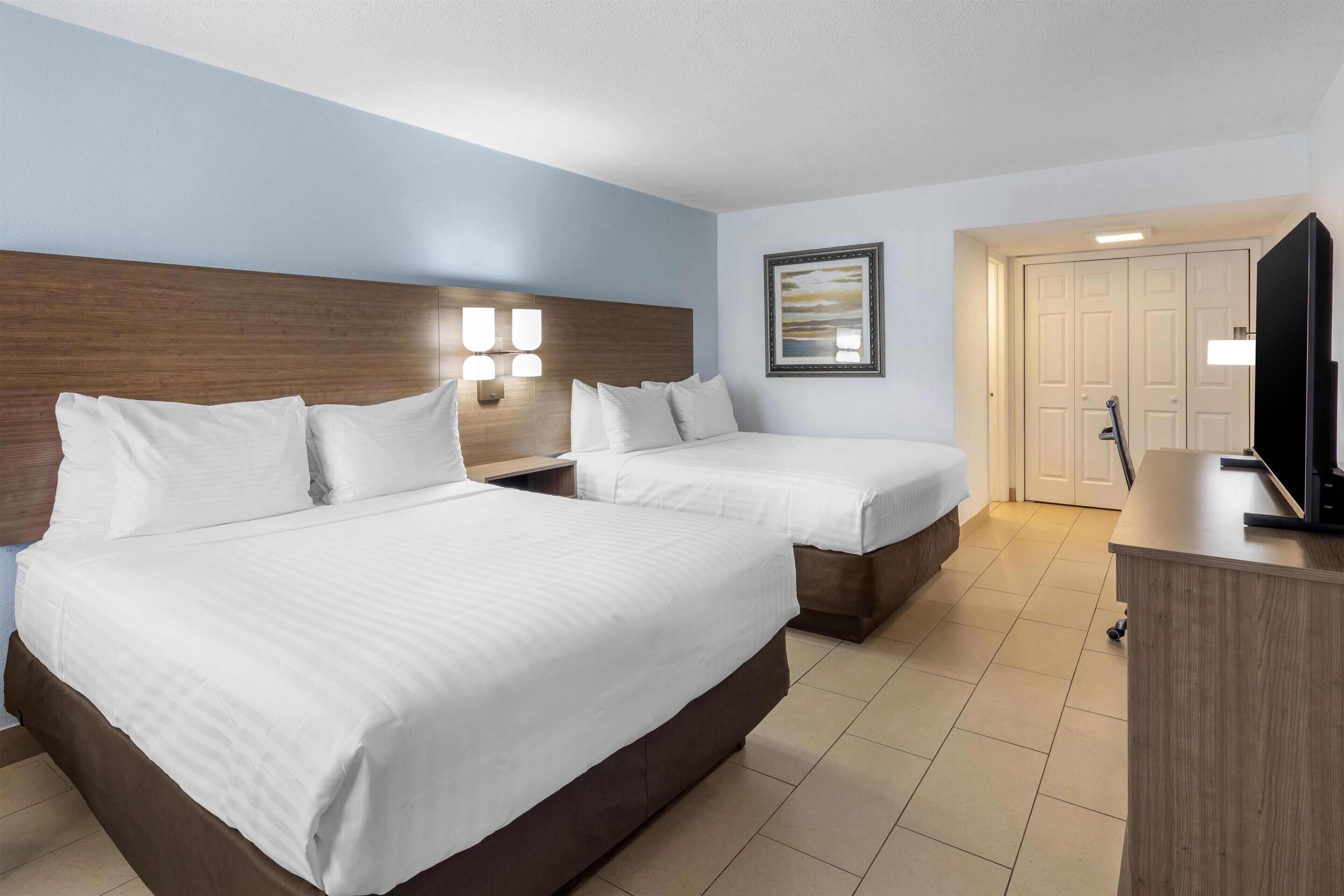 Quarto de hotel com duas camas, uma televisão, uma escrivaninha e uma porta que dá para um armário.