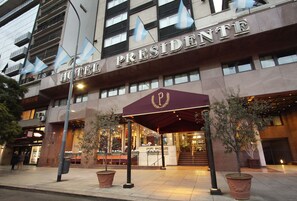 Entrada de hotel com toldo borgonha e placa com a inscrição 'HOTEL PRESIDENTE'.