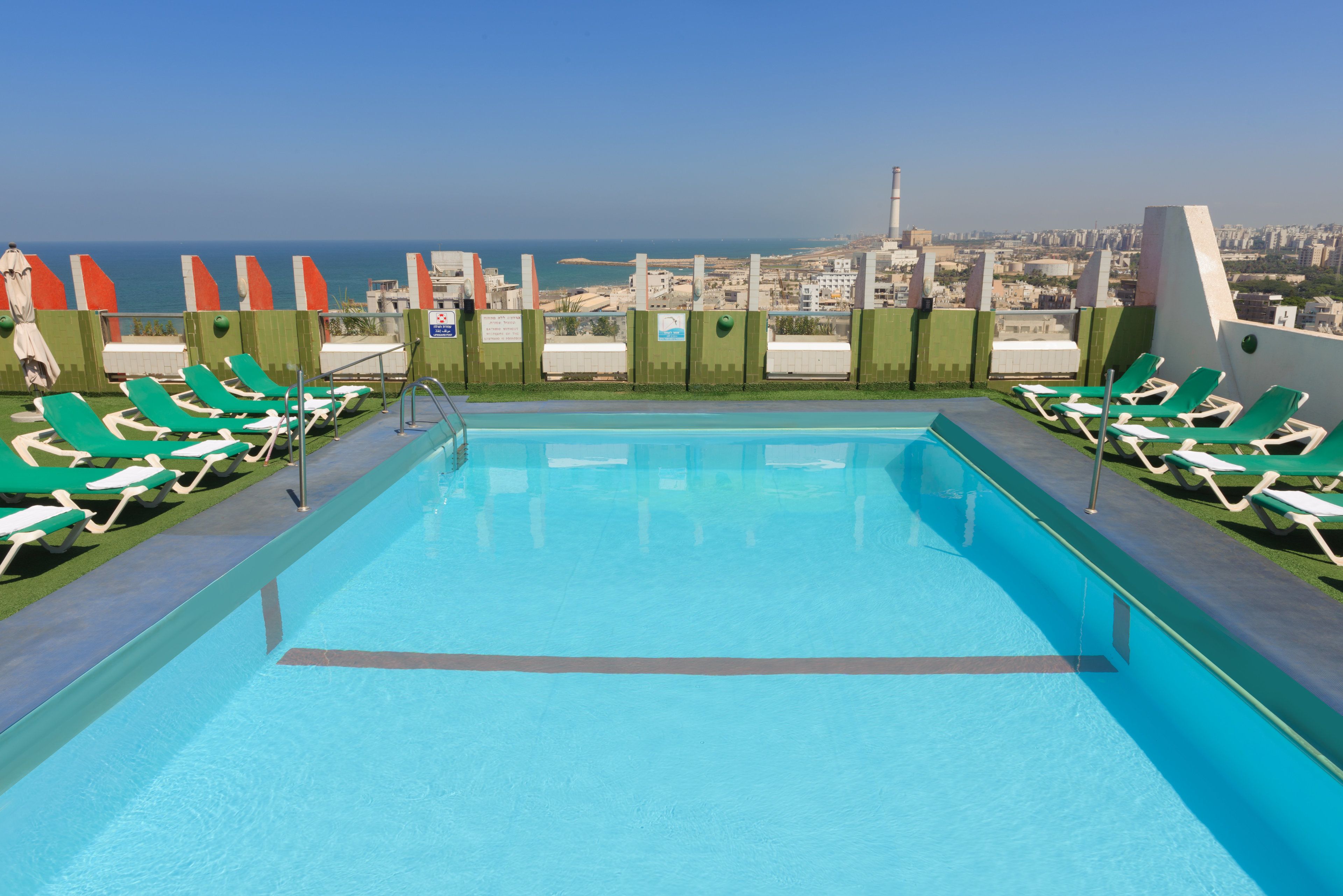 Piscina no terraço com espreguiçadeiras verdes e vista para a cidade.