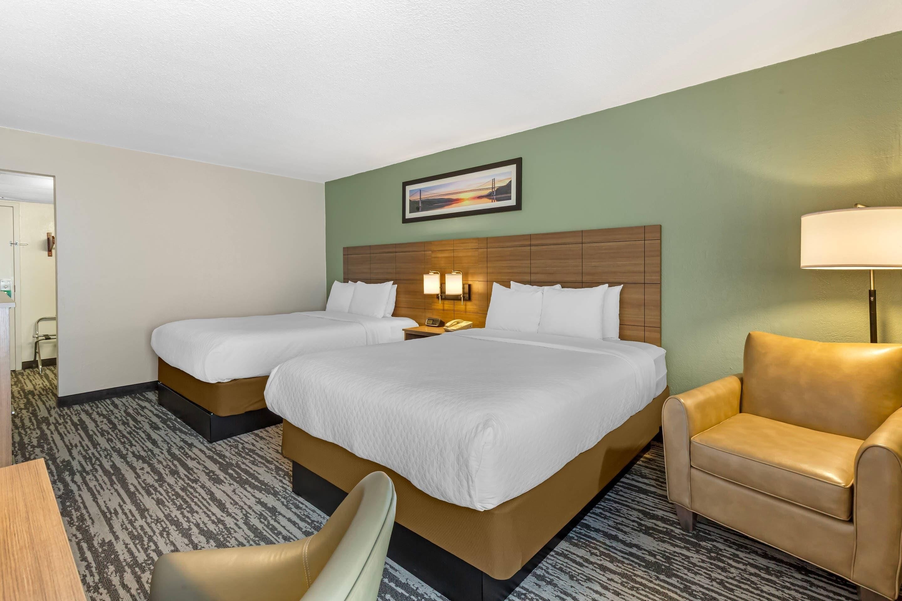 Quarto de hotel com duas camas, uma escrivaninha, uma cadeira e um abajur.