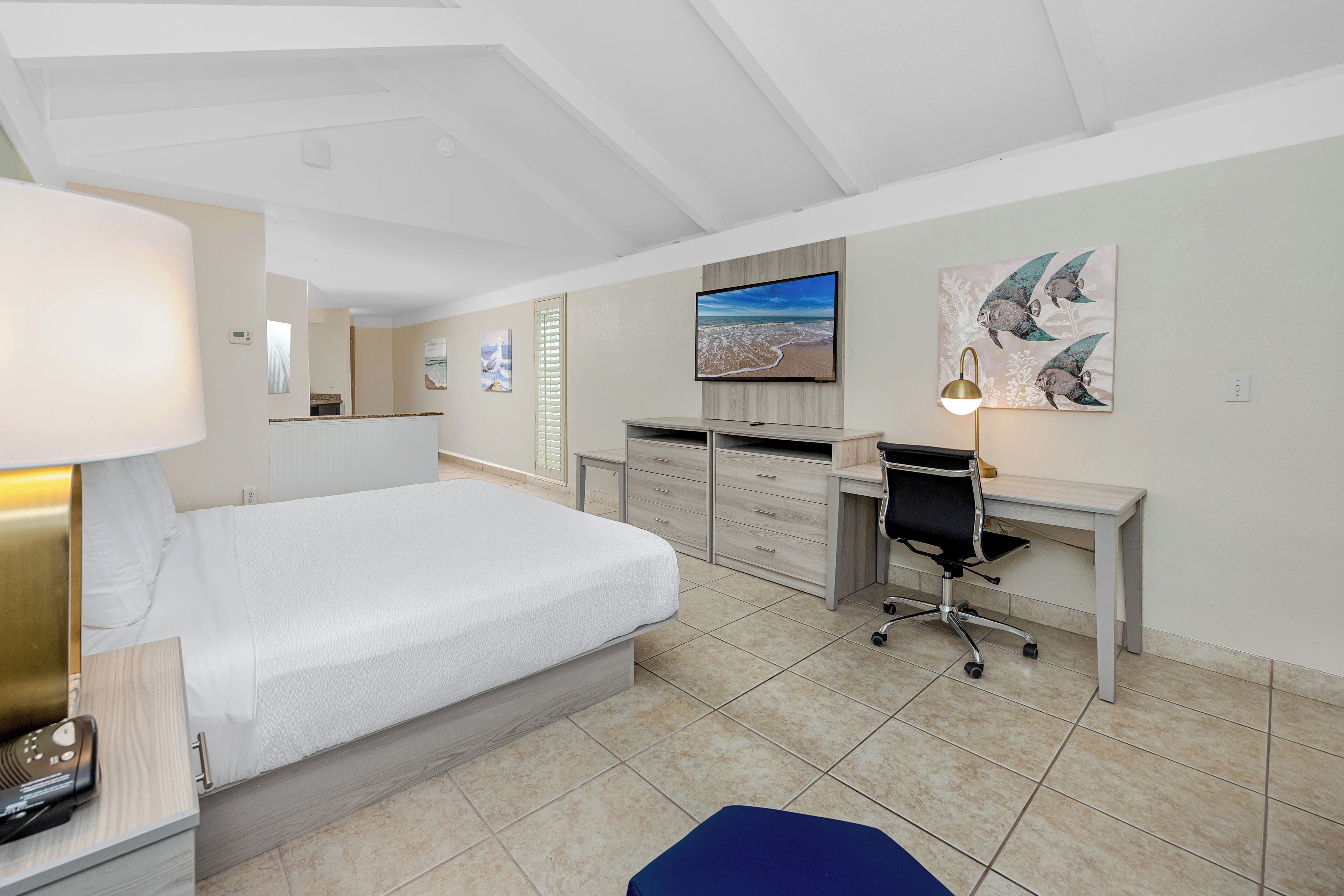 Quarto de hotel com cama, escrivaninha, cadeira e obras de arte nas paredes.
