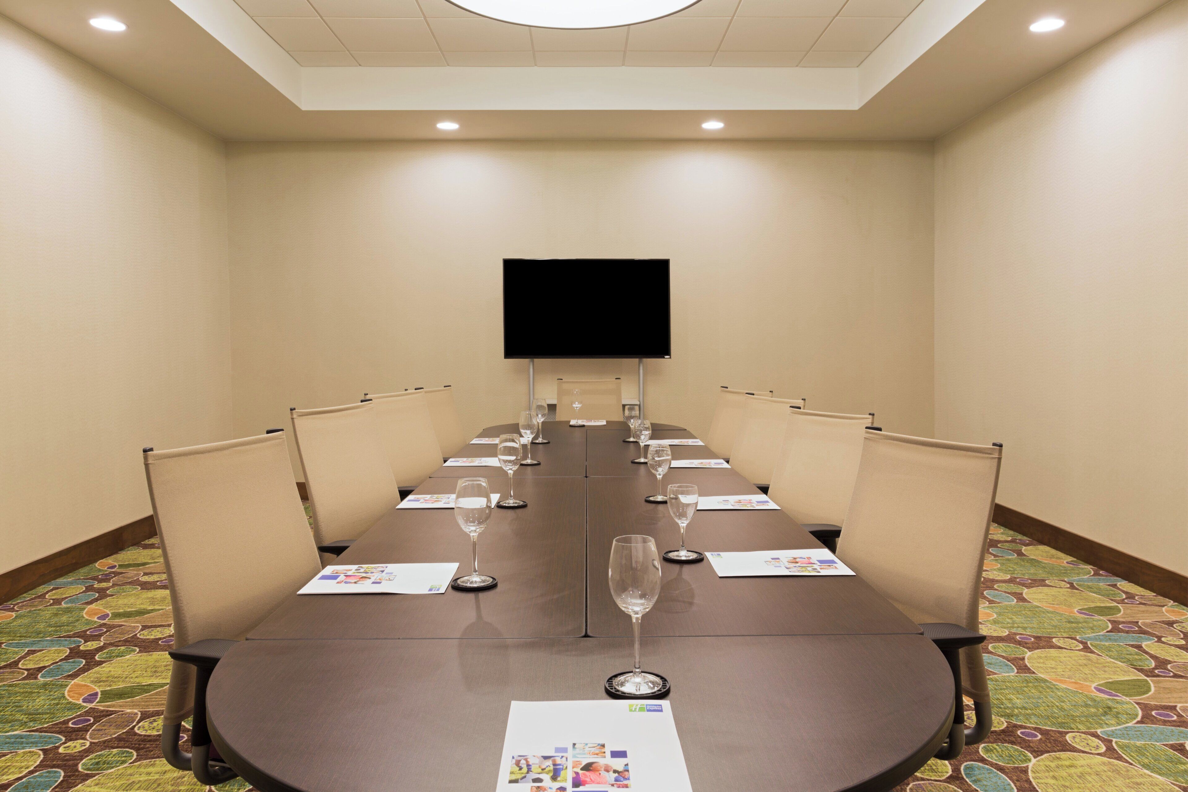 Sala de conferências com uma mesa comprida, cadeiras, uma TV de tela plana e copos.