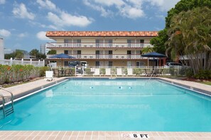 Piscina com marcador de profundidade de 1,47 metros, rodeada por espreguiçadeiras e guarda-sóis, com um edifício alto ao fundo.