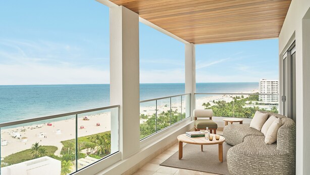 Varanda com vista para a praia e oceano, mobiliada com um sofá, cadeiras e uma mesinha.