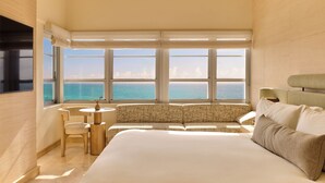 Quarto de hotel com uma cama grande, área de estar e vista para o oceano.