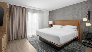 Quarto de hotel moderno com uma cama grande, televisão, escrivaninha com luminária e vista para a cidade.