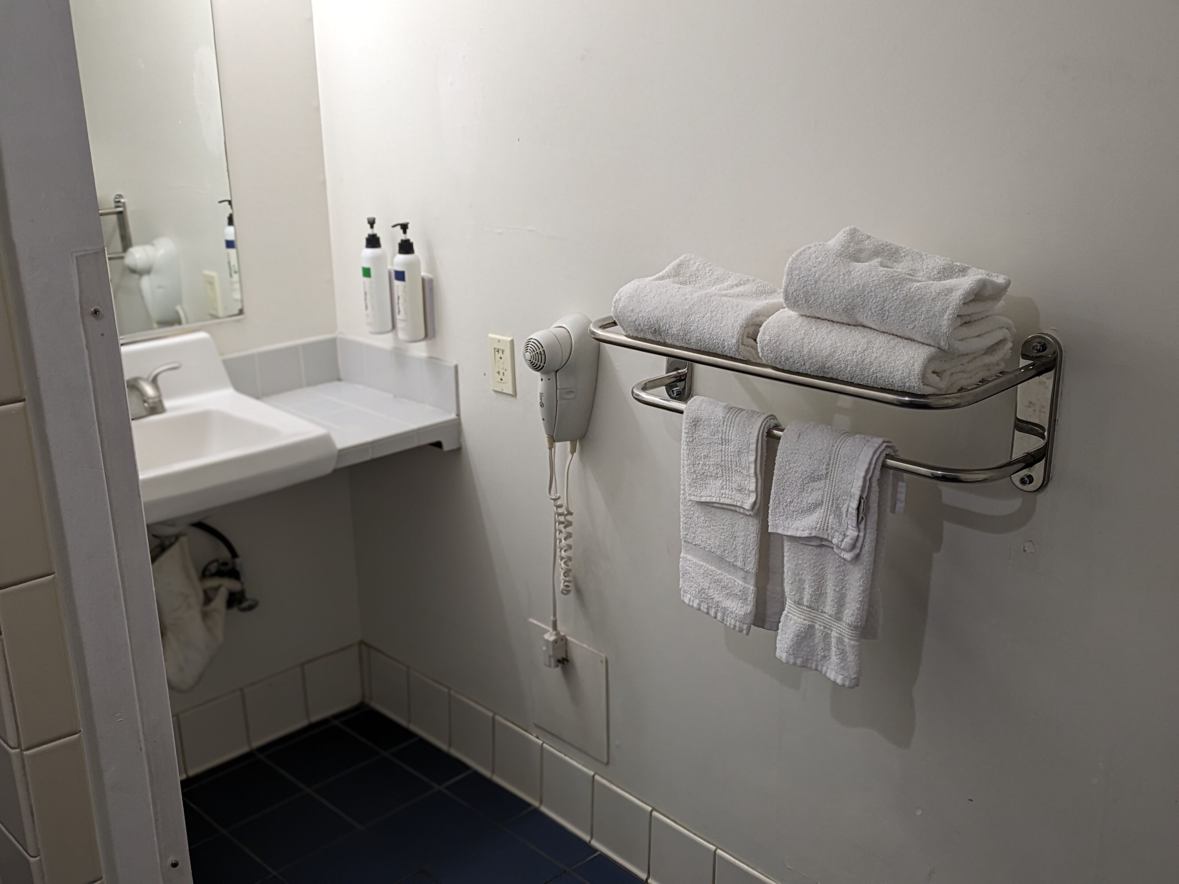 Casa de banho com uma pia branca, um espelho, um porta-toalhas com toalhas dobradas e um secador de cabelo.