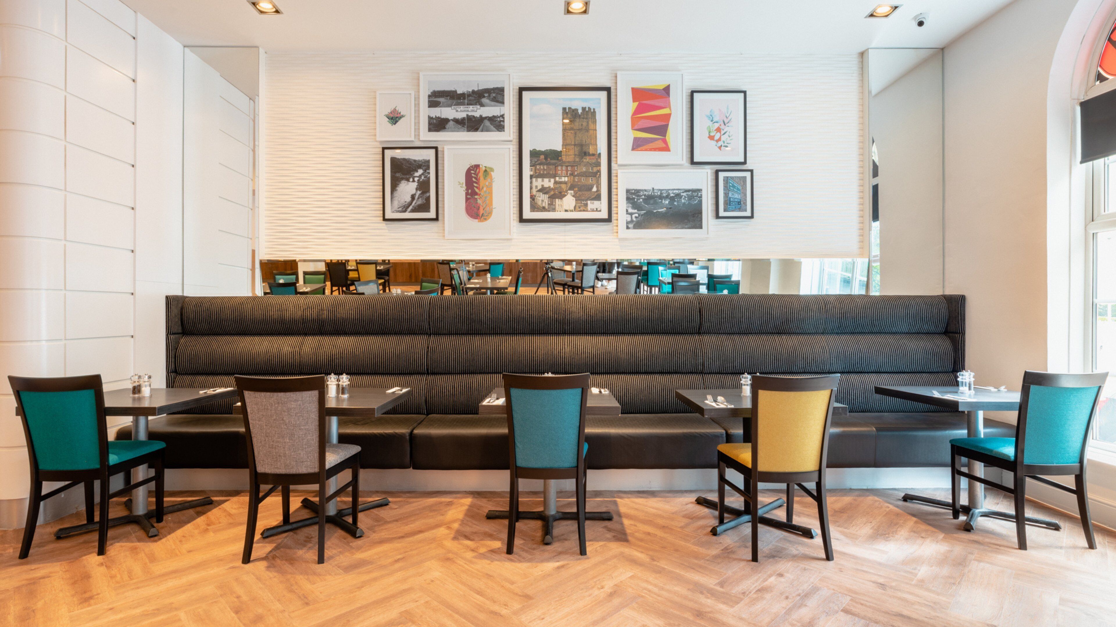 Um restaurante moderno com um amplo banco estofado, várias mesas e cadeiras.