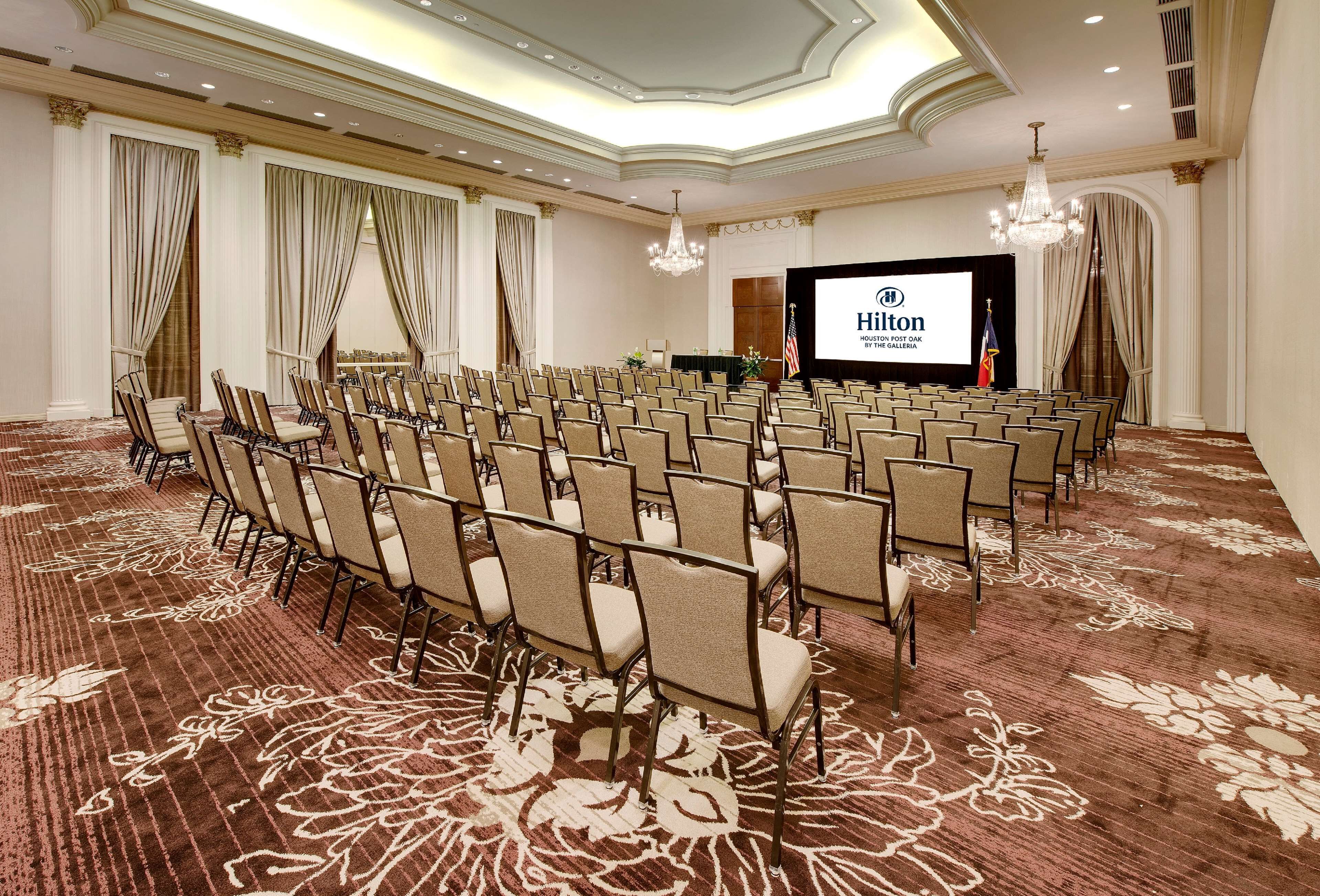 Uma sala de conferências com fileiras de cadeiras voltadas para uma tela exibindo o logotipo da Hilton.