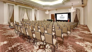 Uma sala de conferências com fileiras de cadeiras voltadas para uma tela exibindo o logotipo da Hilton.