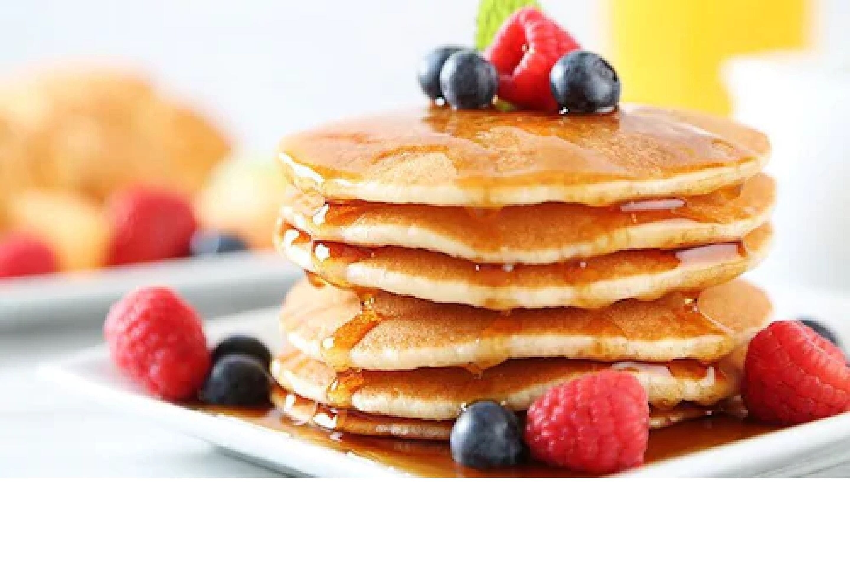 Uma pilha de panquecas com calda e frutos vermelhos.