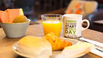 Uma mesa de café da manhã com um croissant, uma tigela de frutas, um copo de suco de laranja e uma caneca com uma mensagem.