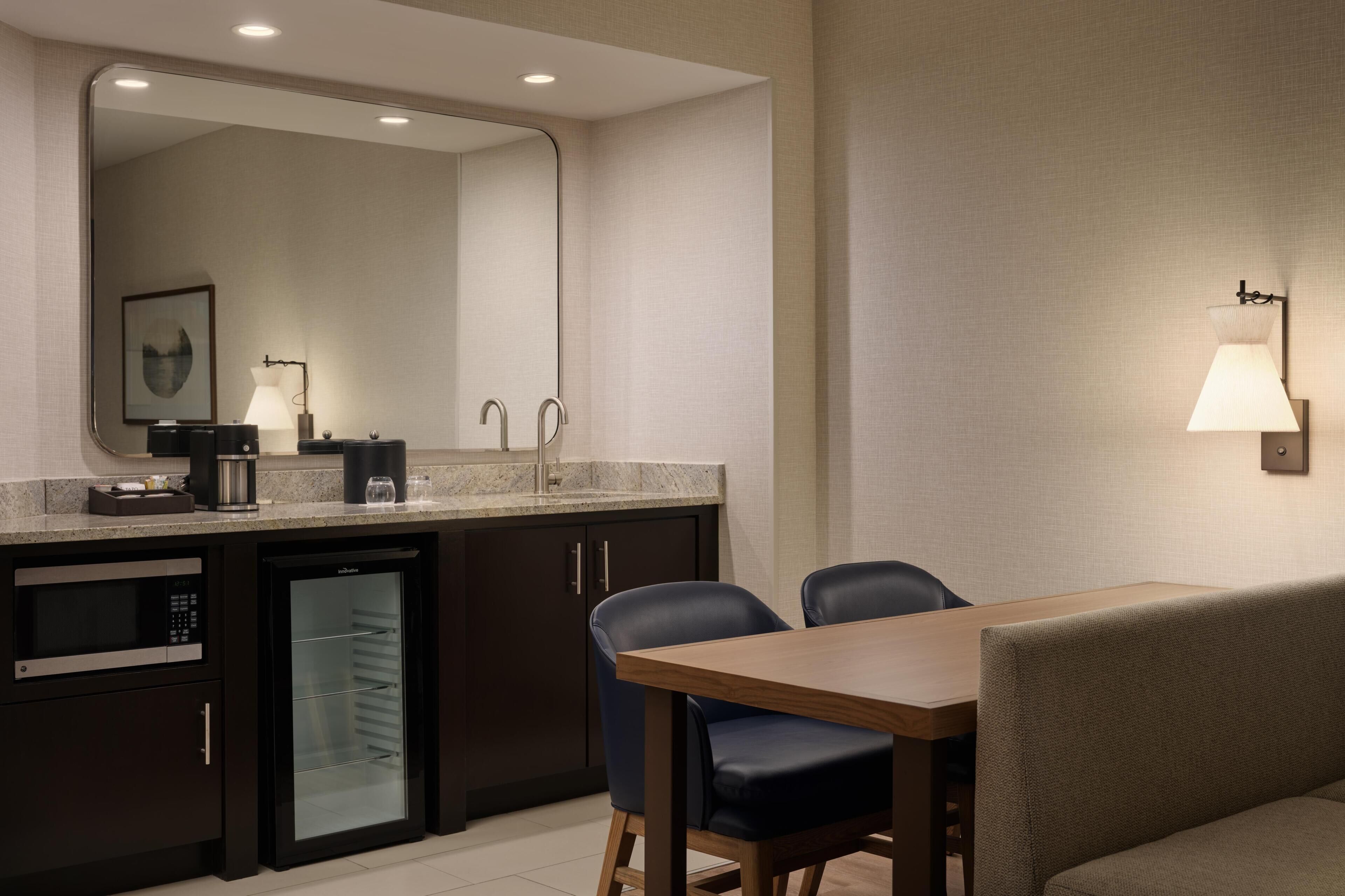 Cozinha compacta com micro-ondas, geladeira e pia. Há uma área de jantar com mesa e cadeiras.
