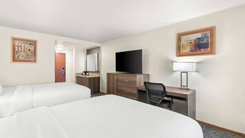 Quarto de hotel com duas camas, uma escrivaninha com cadeira, televisão e dois quadros nas paredes.