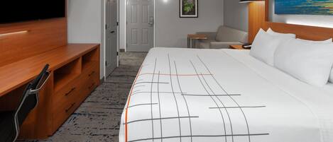 Quarto de hotel com uma cama grande, uma mesa com cadeira, uma televisão, um quadro e uma porta que dá para outro quarto.