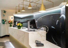 Um balcão de recepção com computador, telefone e flores decorativas.