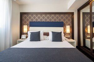 Quarto de hotel com uma cama grande, duas mesas de cabeceira, um criado-mudo, um espelho e cabeceira estampada.