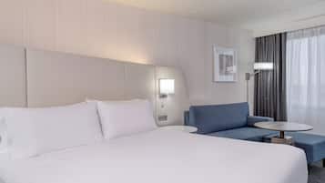 Quarto de hotel com cama grande, sofá, mesa pequena e luminária de parede.