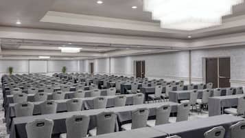 Uma sala de conferências com fileiras de mesas e cadeiras, um lustre e um quadro branco.