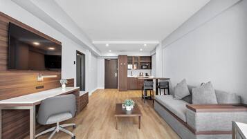 Uma sala de estar moderna com escrivaninha de madeira, sofá cinzento e uma pequena mesa com uma planta.