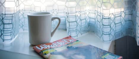 Uma caneca branca e uma revista sobre um peitoril.