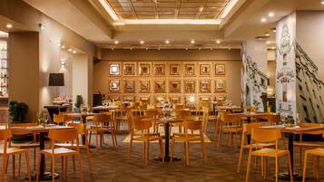 Um restaurante amplo com várias mesas e cadeiras, teto com iluminação embutida e parede decorada com quadros.